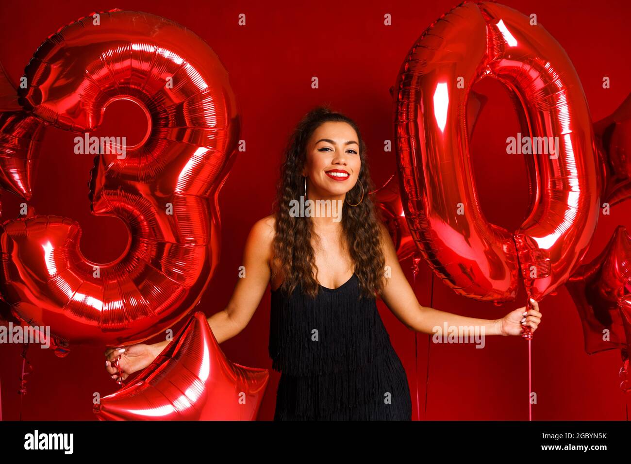 Portrait of happy 30 year old woman on red background with red balloons ...