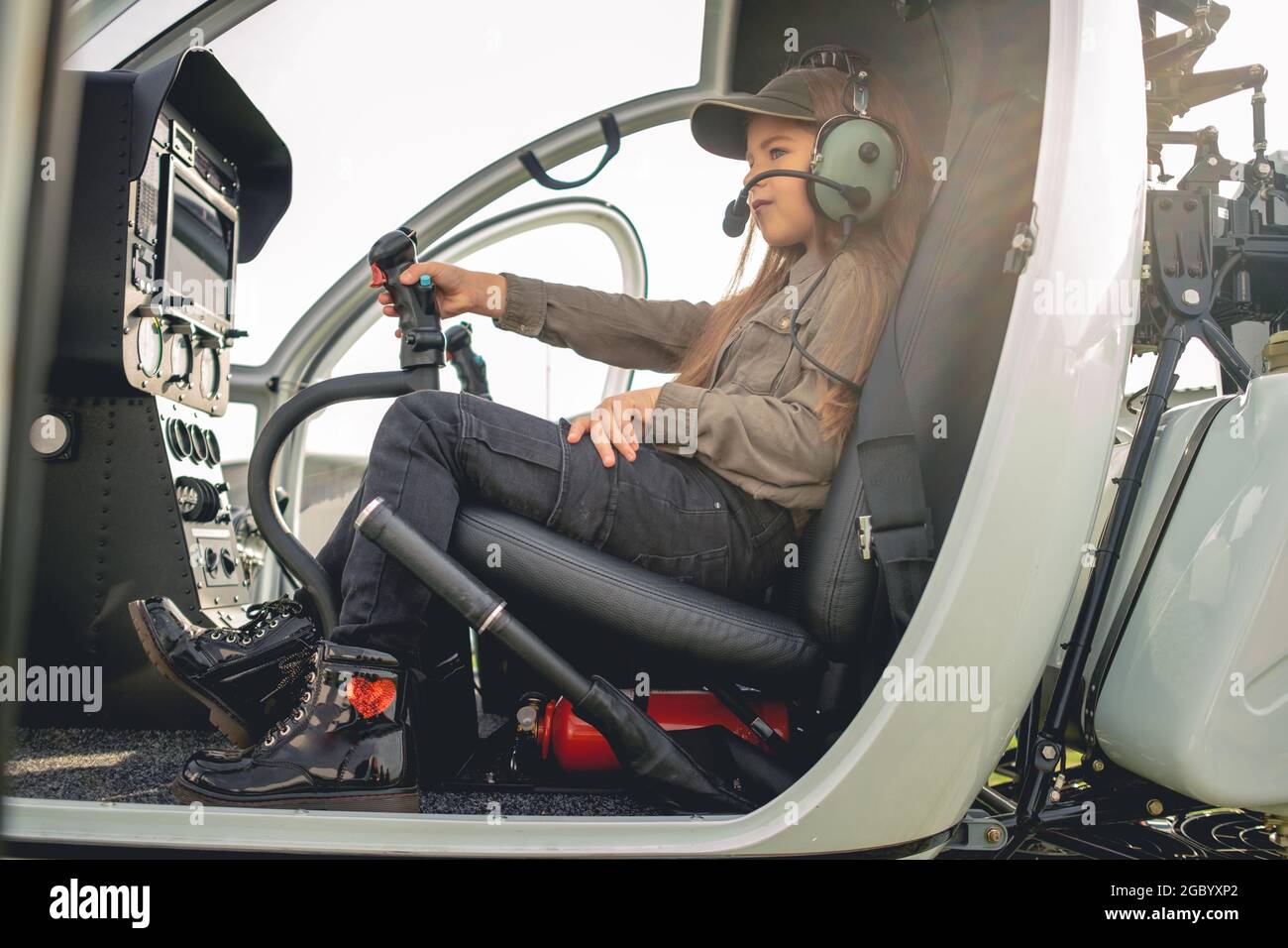 Focused preteen girl in aviator headset sitting in helicopter cockpit ...
