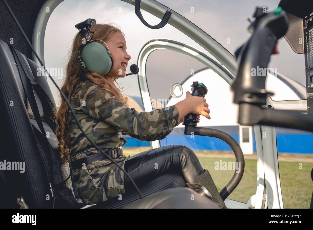 Smiling tween girl in aviator headset sitting in helicopter cockpit ...