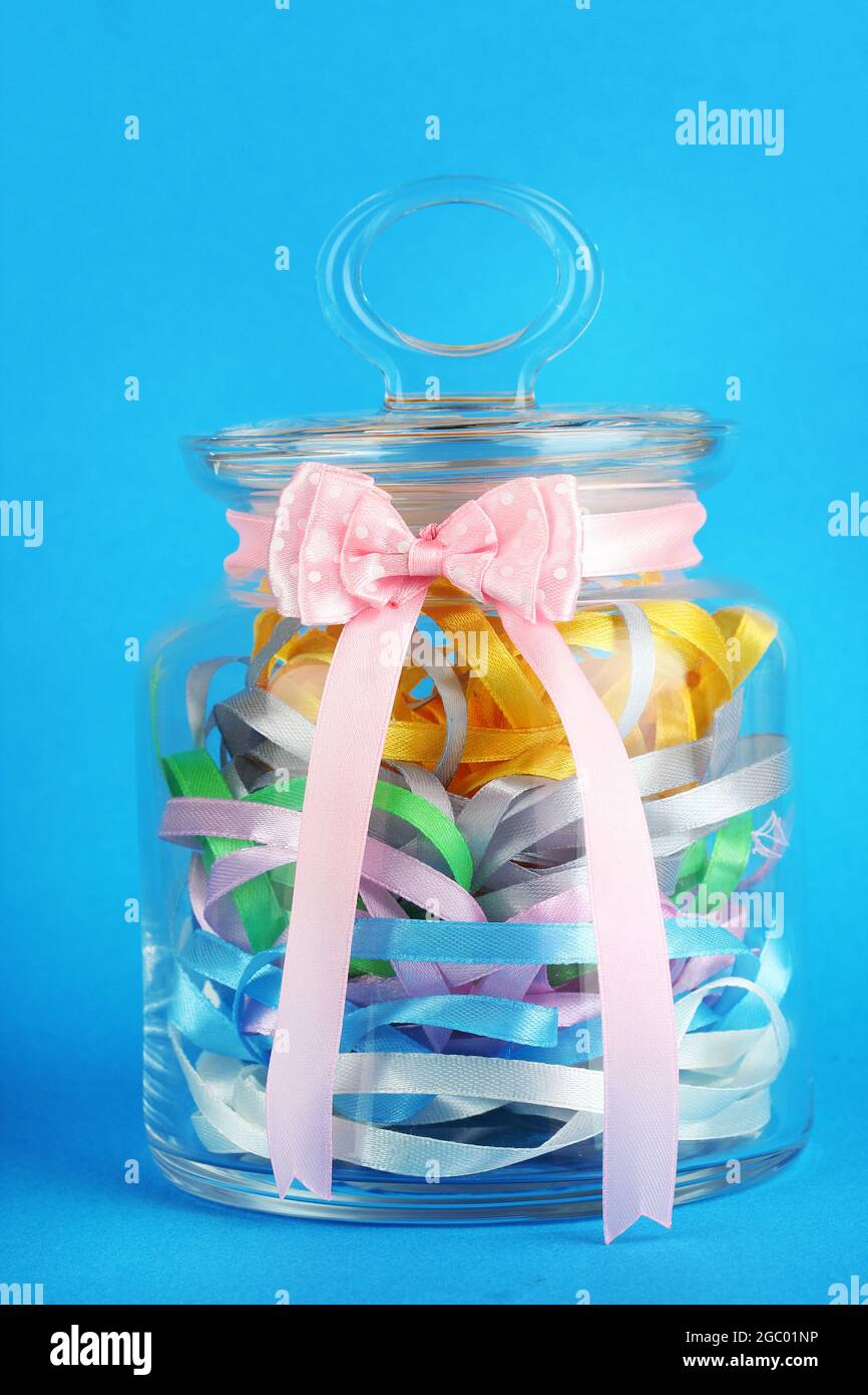 Glass jar containing various colored ribbons on blue background Stock ...