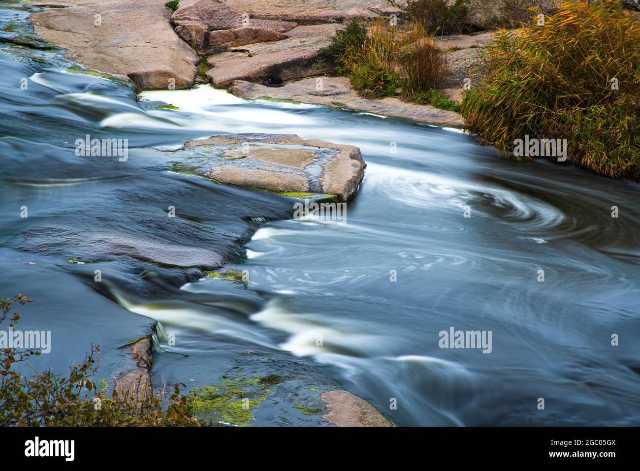 A small shining stream flows among smooth wet and dark stones Stock ...