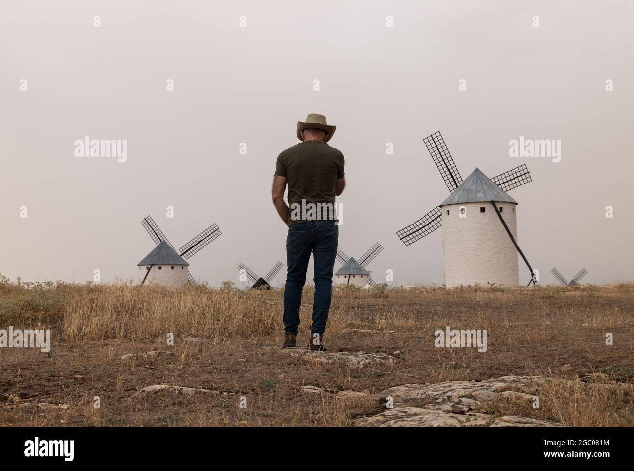 A man wearing a cowboy hat with windmills in the countryside Stock ...