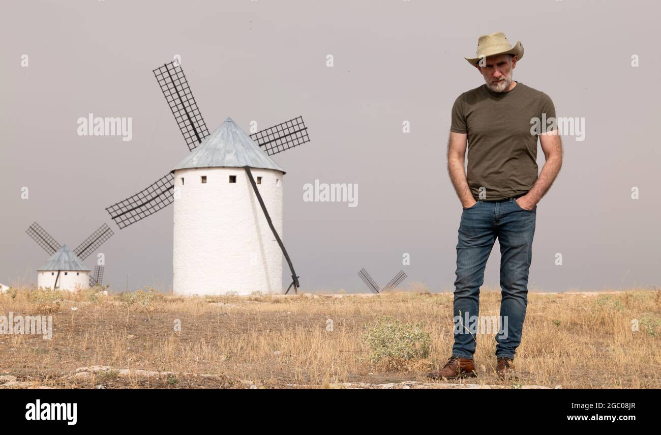 A man wearing a cowboy hat with windmills in the countryside Stock ...