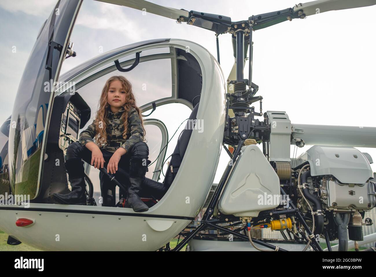 Tween girl in camouflage style tunic sitting in open helicopter cockpit ...