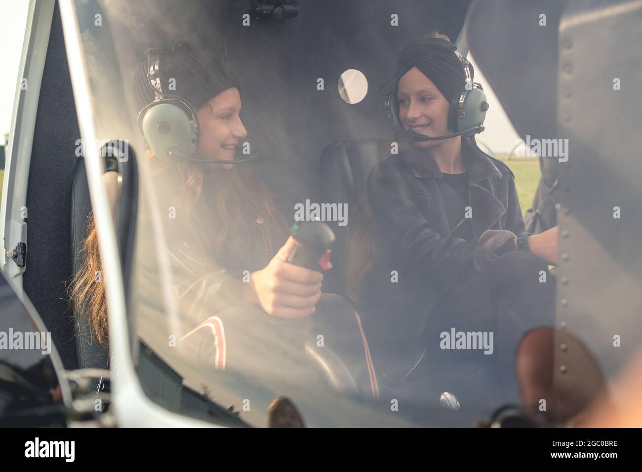 Two happy teen girls in pilot headsets talking in helicopter cockpit ...