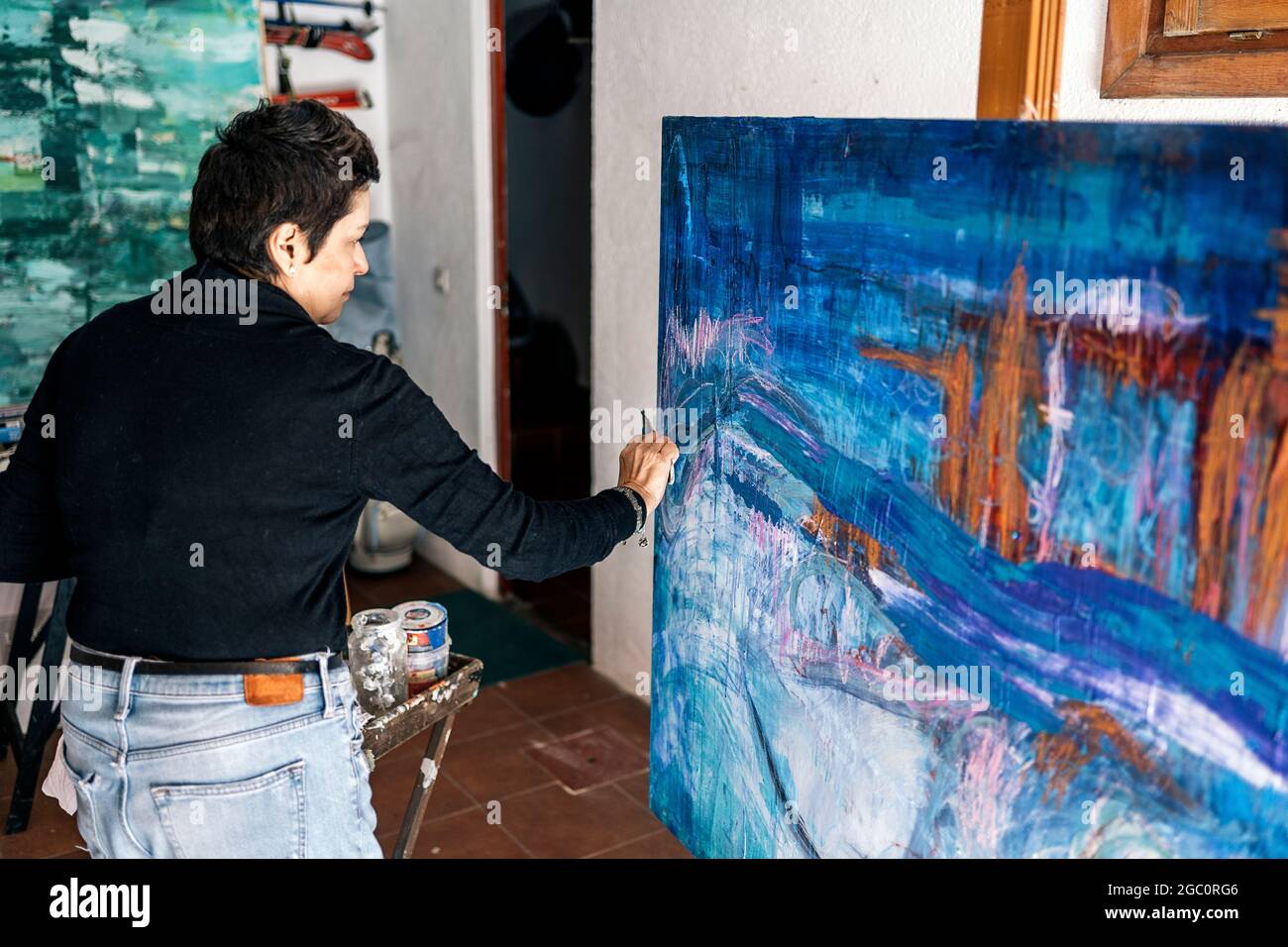Focused female painter painting with blue colors an abstract art piece ...