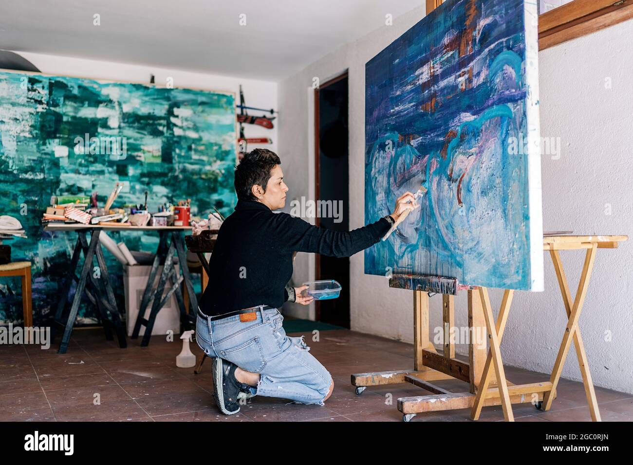 Focused middle aged painter working in her home art studio and using ...