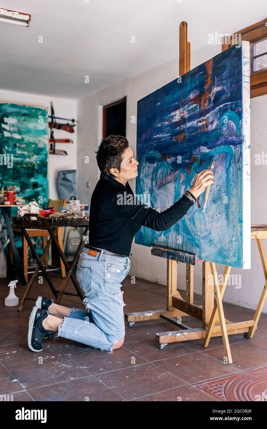 Focused middle aged painter working in her home art studio and using ...