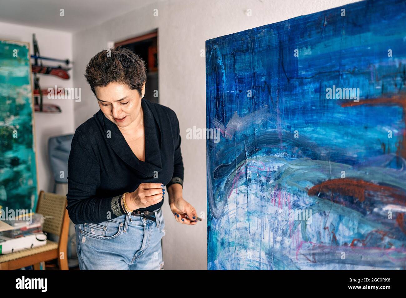 Happy female painter relaxing in her garage painting with blue paint in ...