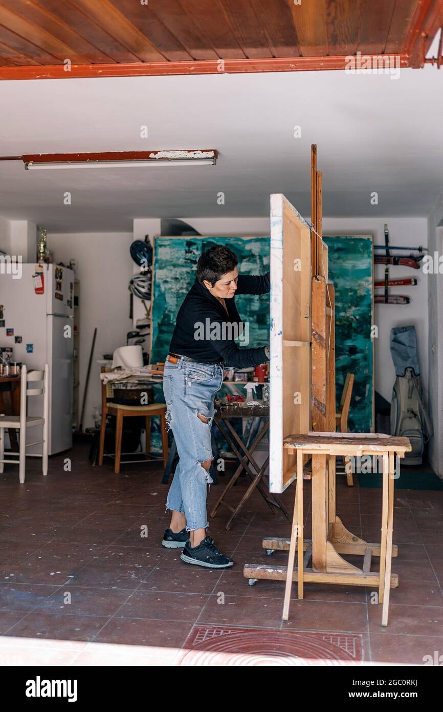 Focused middle aged artist painting in big canvas. She has an art ...