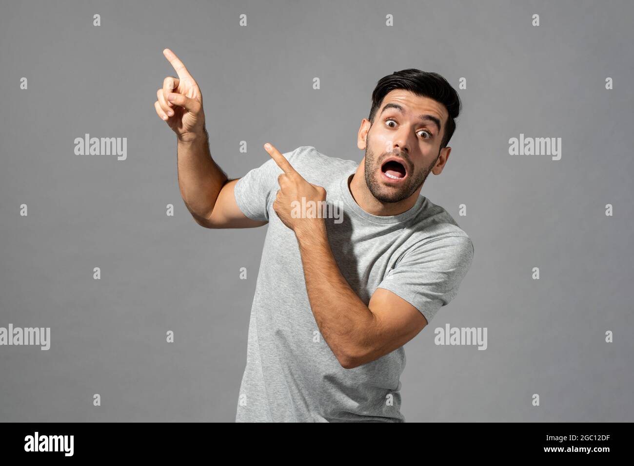 Shocked young Caucasian man with hands pointing up in isolated light ...