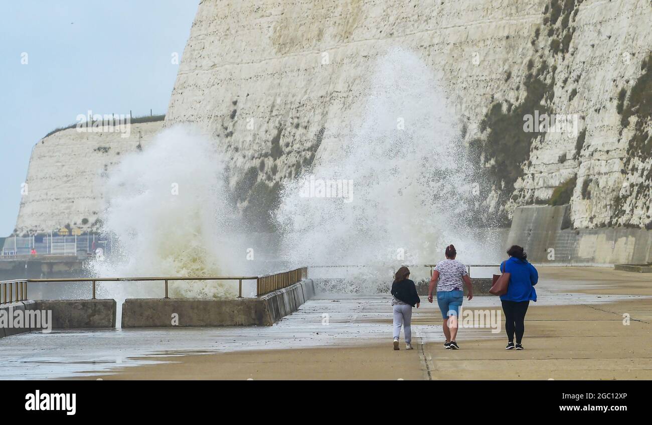 Brighton UK 6th August 2021 - Walkers pass by as huge waves crash over ...