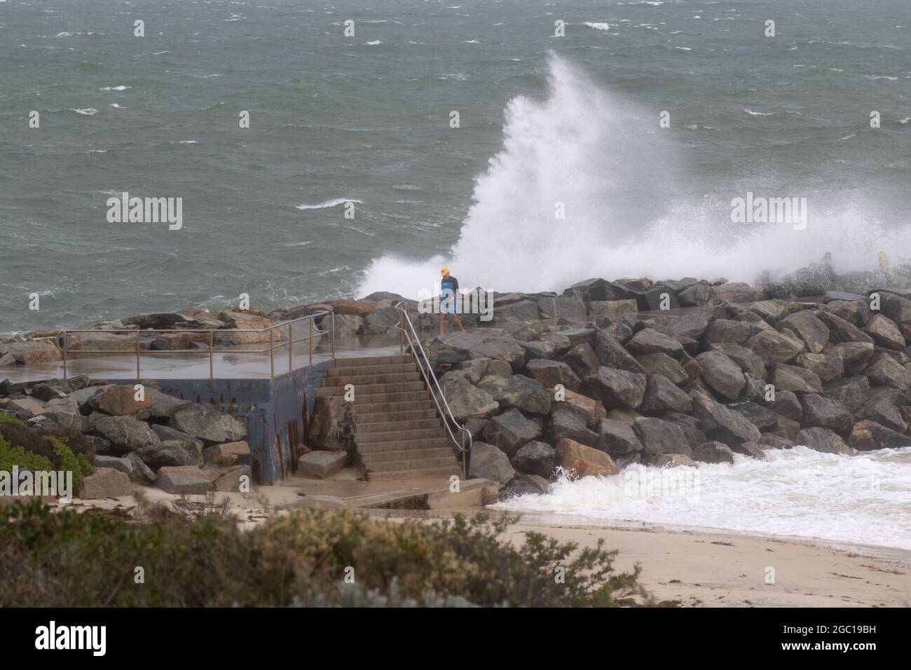 Man walking on pier about to be soaked by crashing wave Stock Photo - Alamy