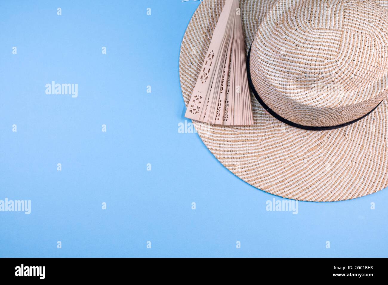 Top view of a straw hat with black ribbon and fan isolated on blue ...