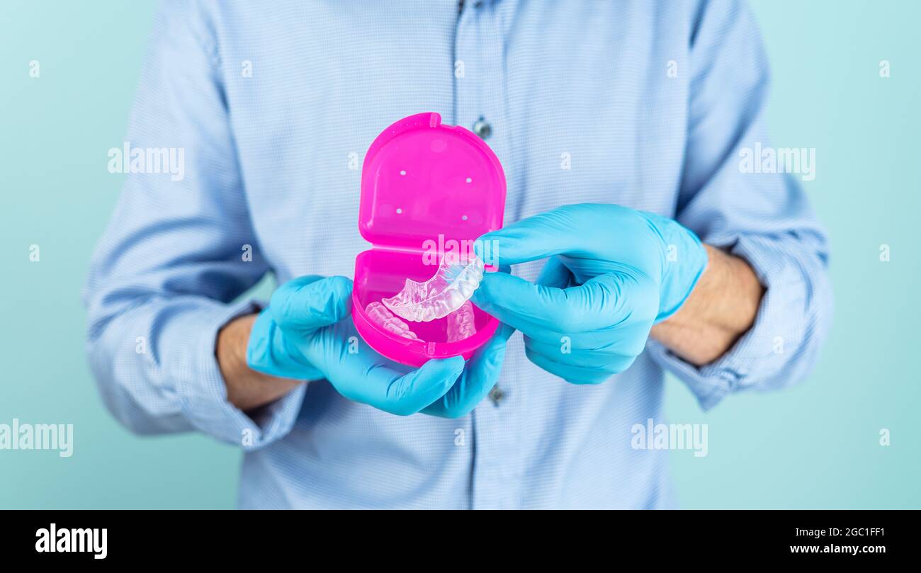 Doctor in blue shirt and gloves showing a dental splint in pink box ...