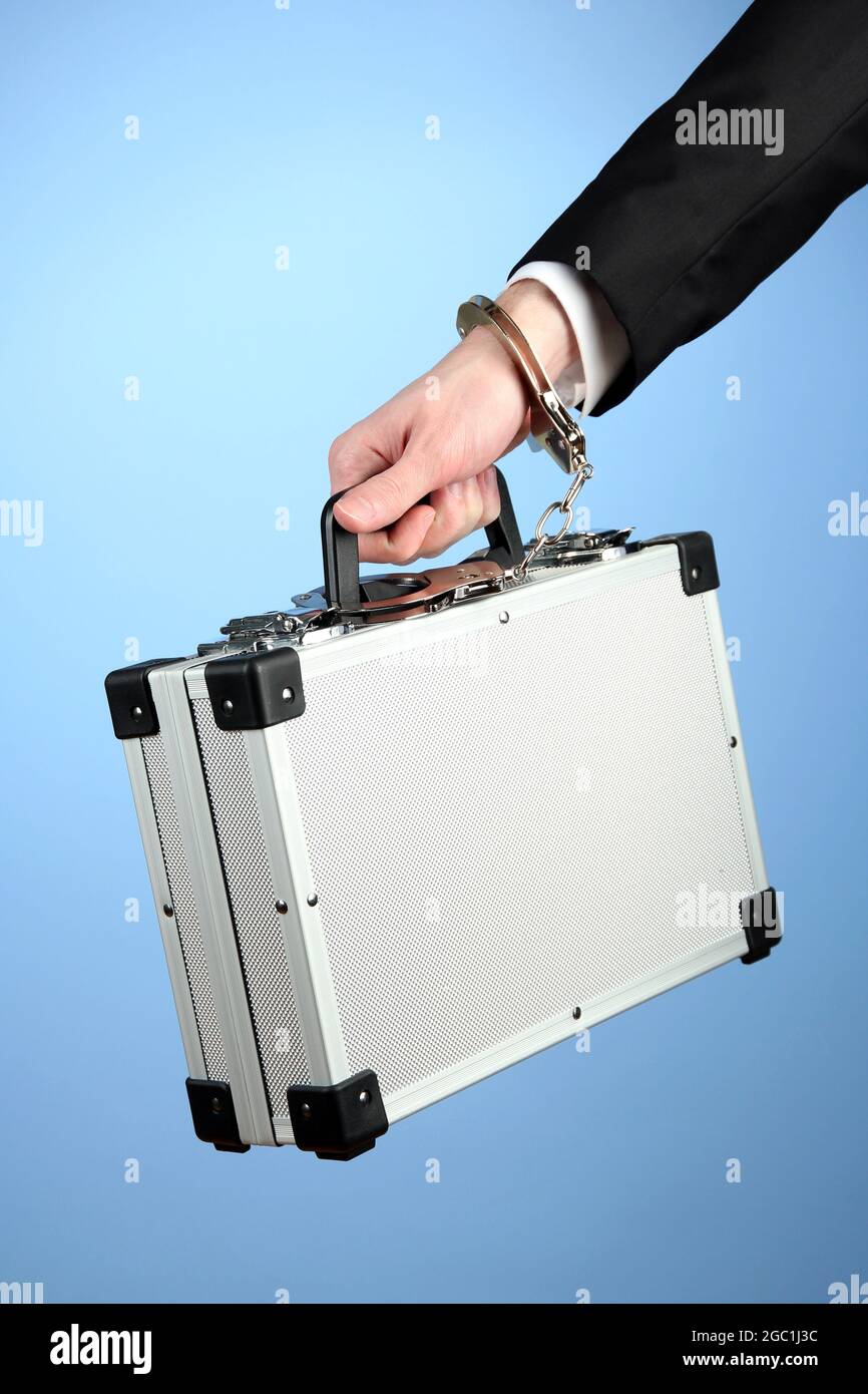 Hand with handcuff and suitcase, on color background Stock Photo - Alamy