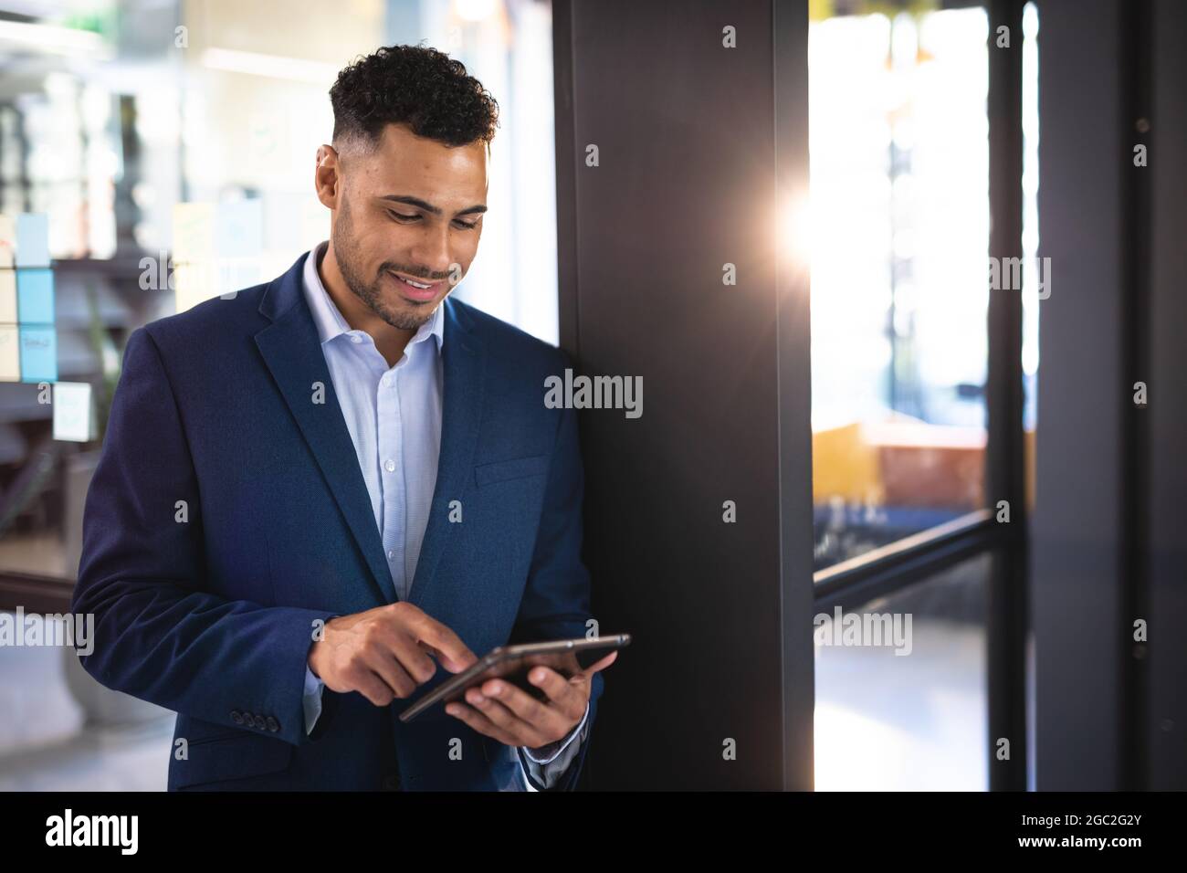 Smiling mixed race businessman using tablet and wearing navy jacket ...