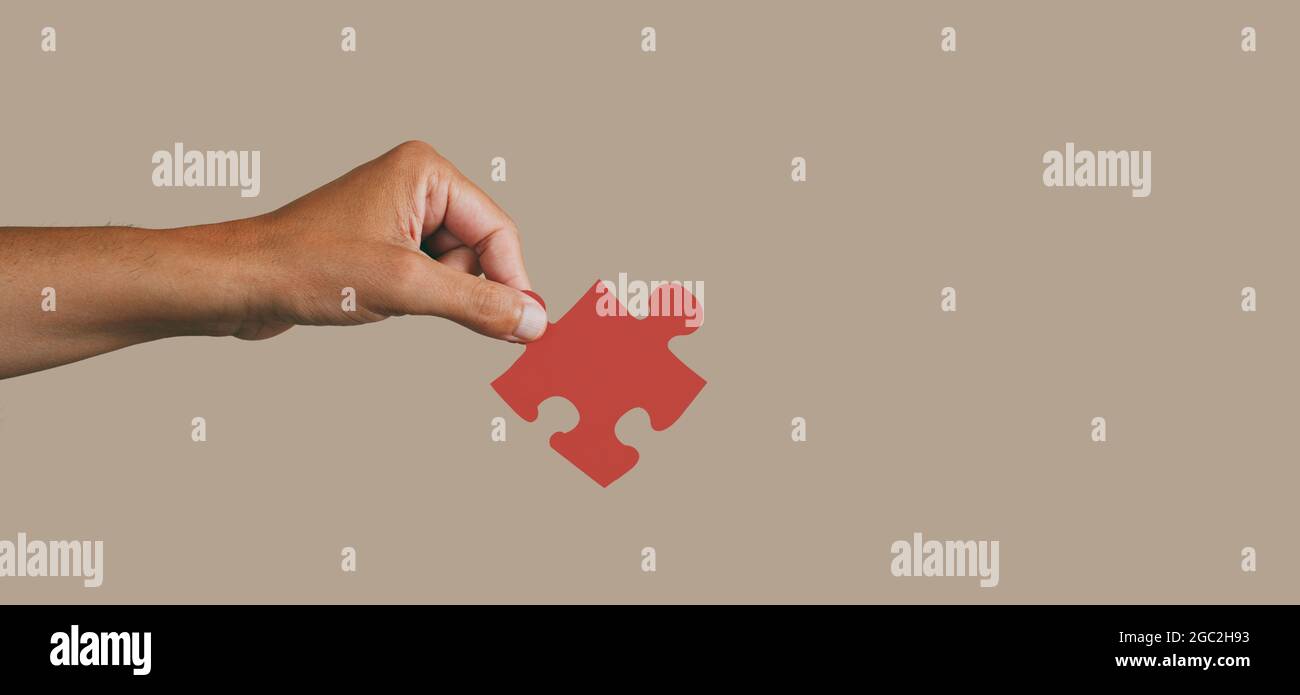 a young caucasian man has a red puzzle piece in his hand, on a pale ...