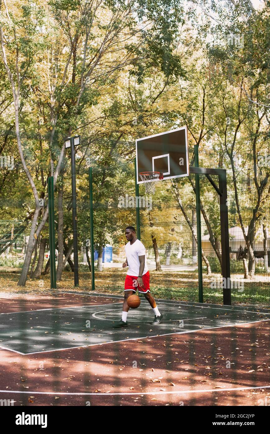 Young black smiling man playing basketball on the court at sunrise ...