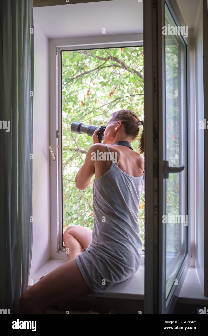 Photographer with a camera in his hands sits on a windowsill by an open ...