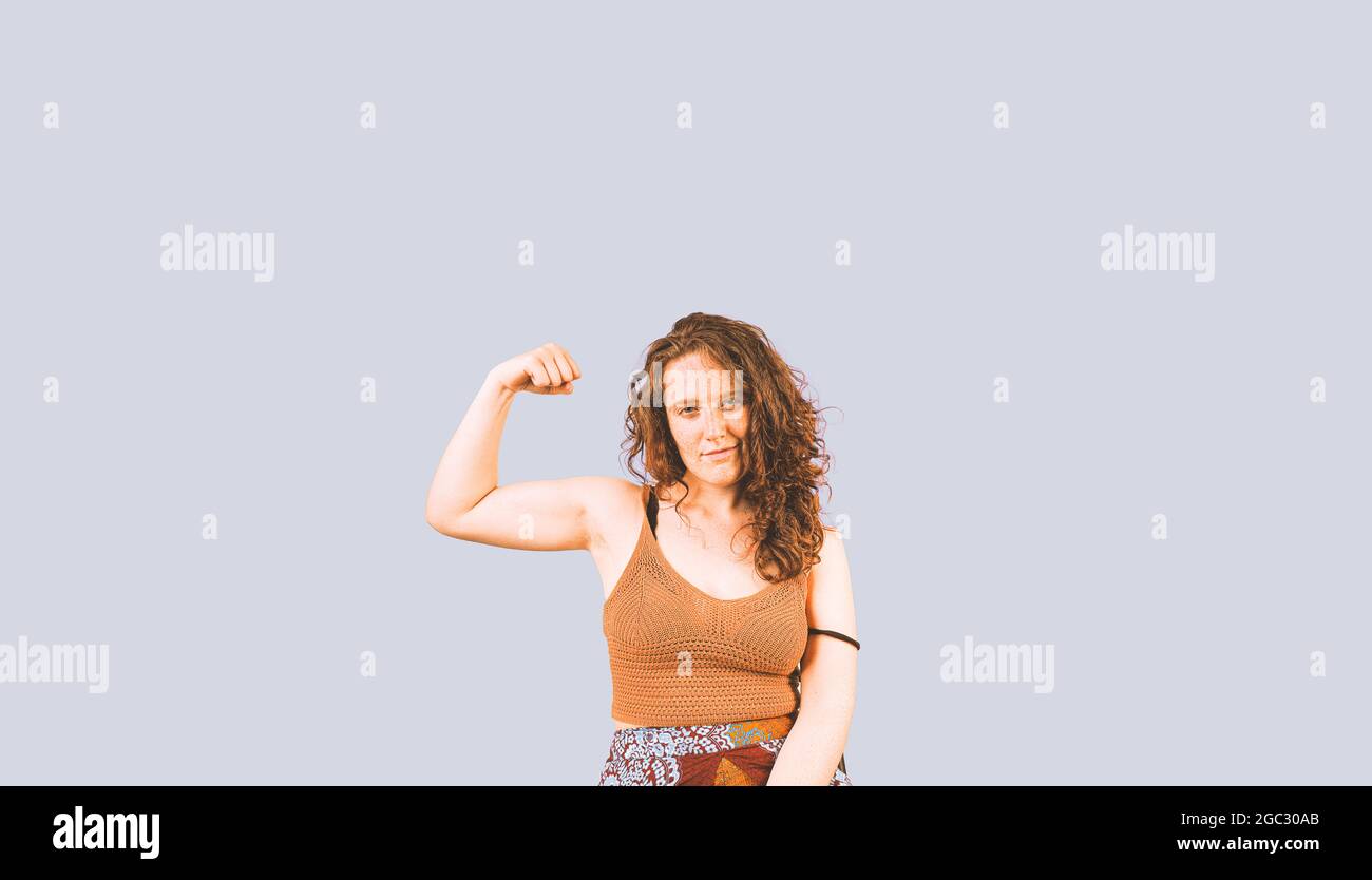 Young ginger female posing showing off her muscles on a gray background ...