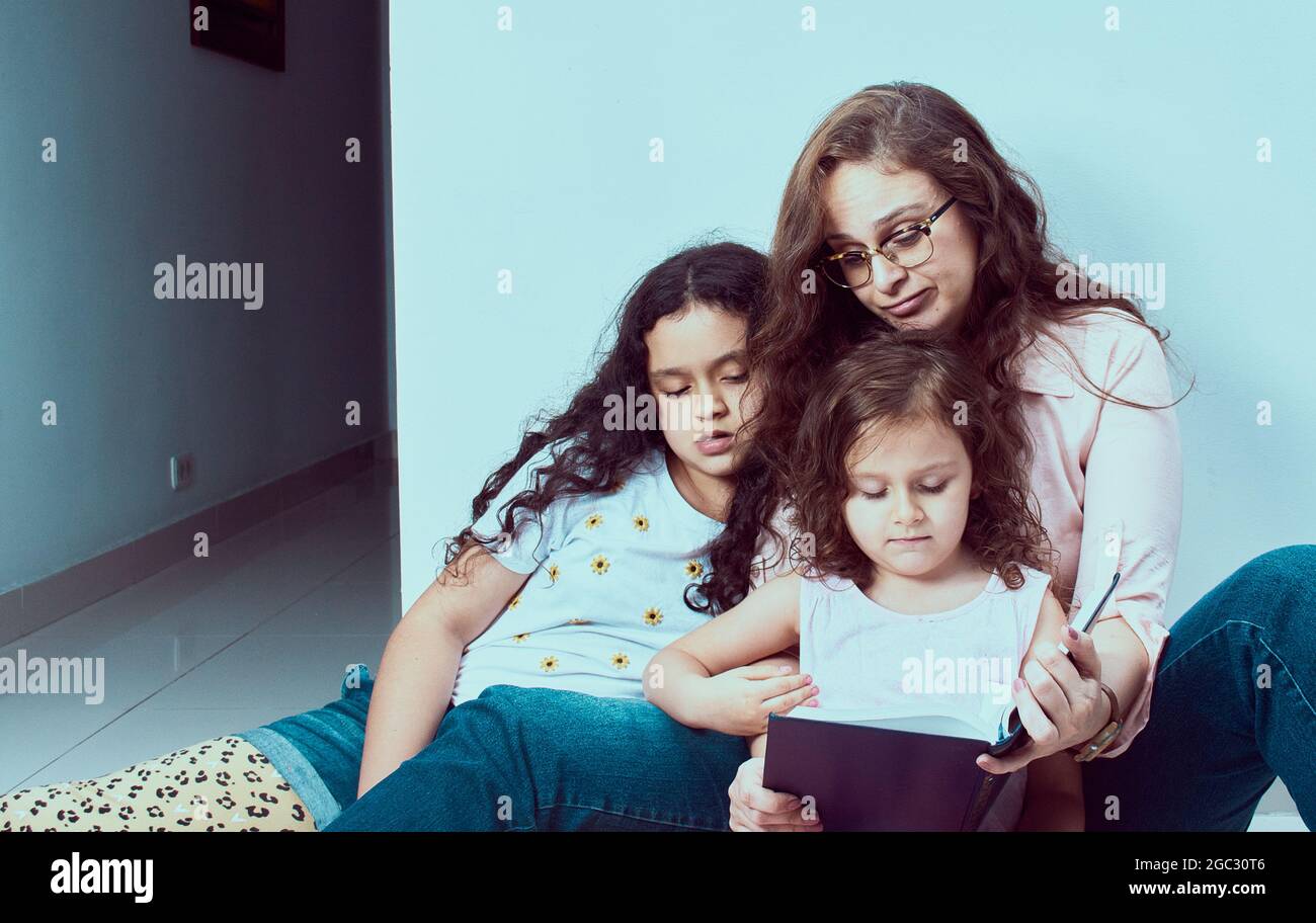 Three girls reading a book sitting near the wall Stock Photo - Alamy