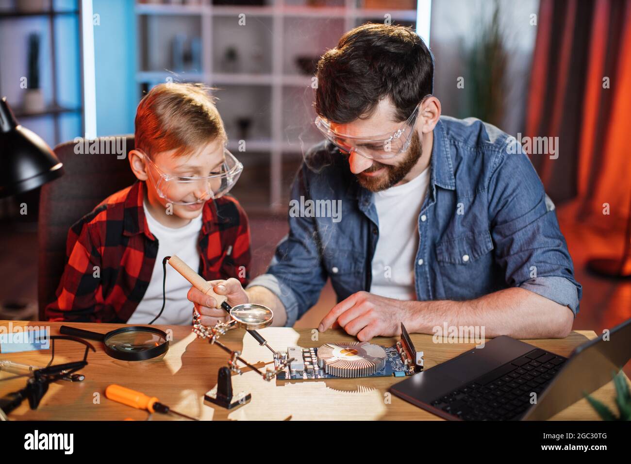 Happy little boy and his father sitting together at table and repairing ...