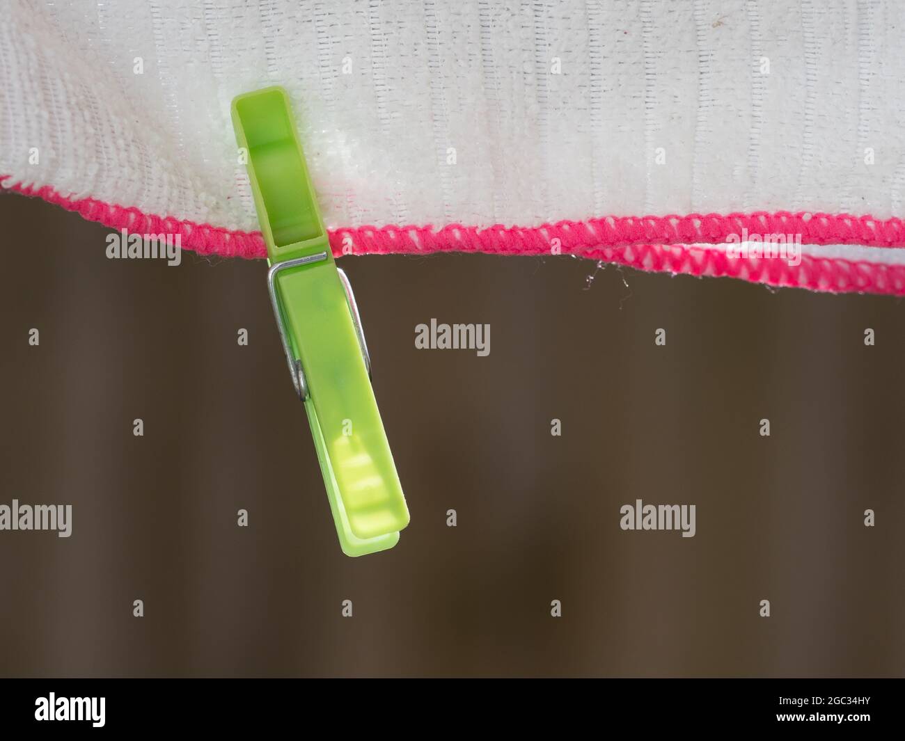 A lime green clothes peg is pegged to a white cloth with pink edging ...