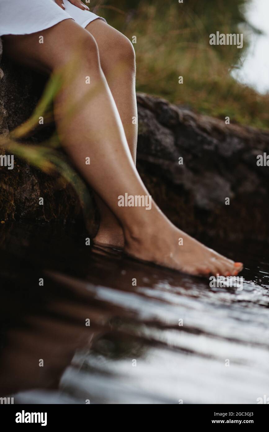 Vertical shot of a woman dipping her legs in the lake, in nature during ...
