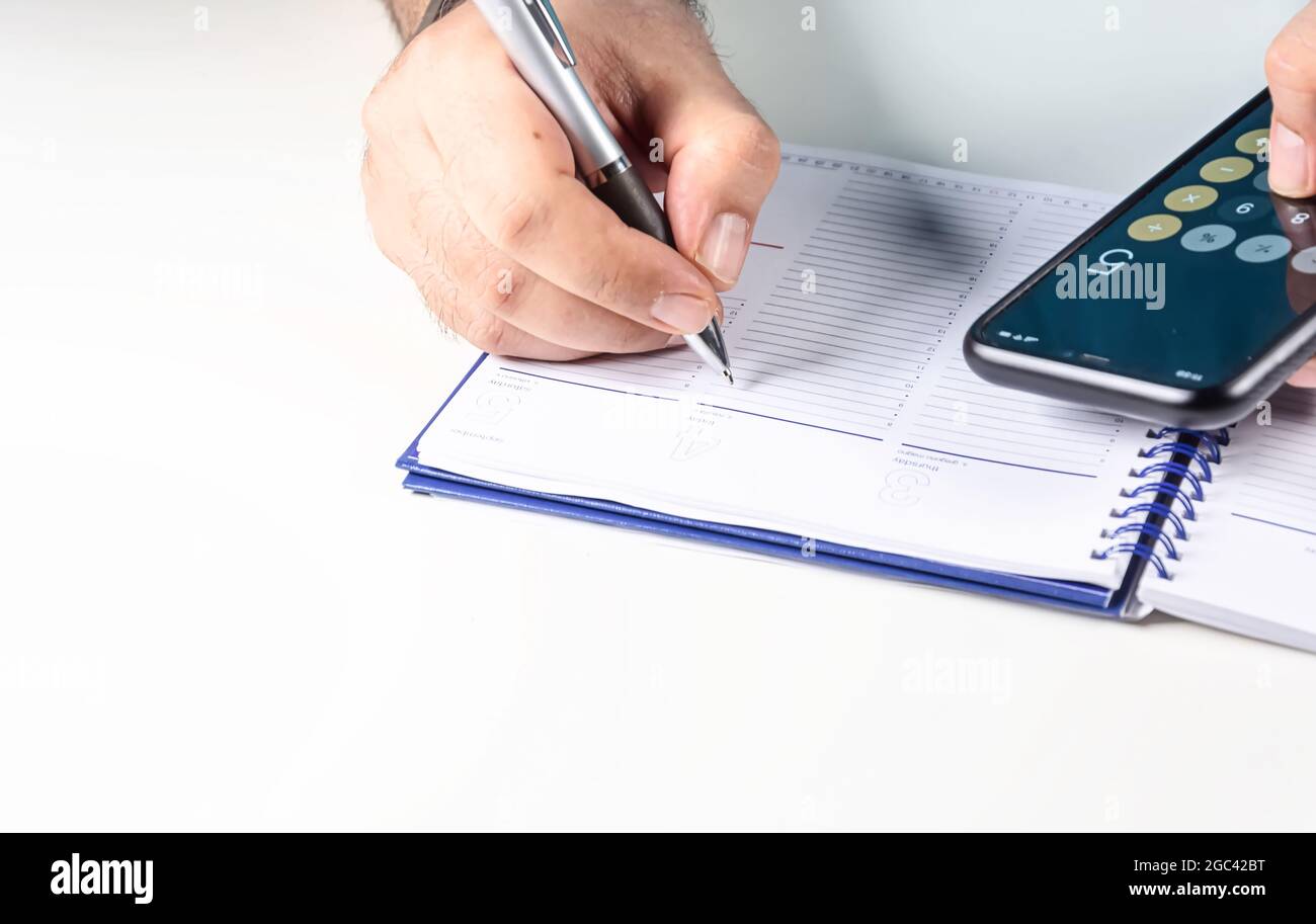 Man doing calculations with his mobile phone calculator and writing in ...
