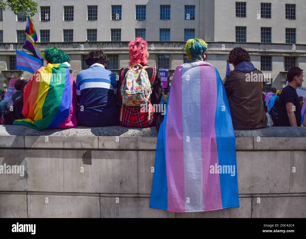Protesters wrapped in pride and trans pride flags sit on a wall during ...