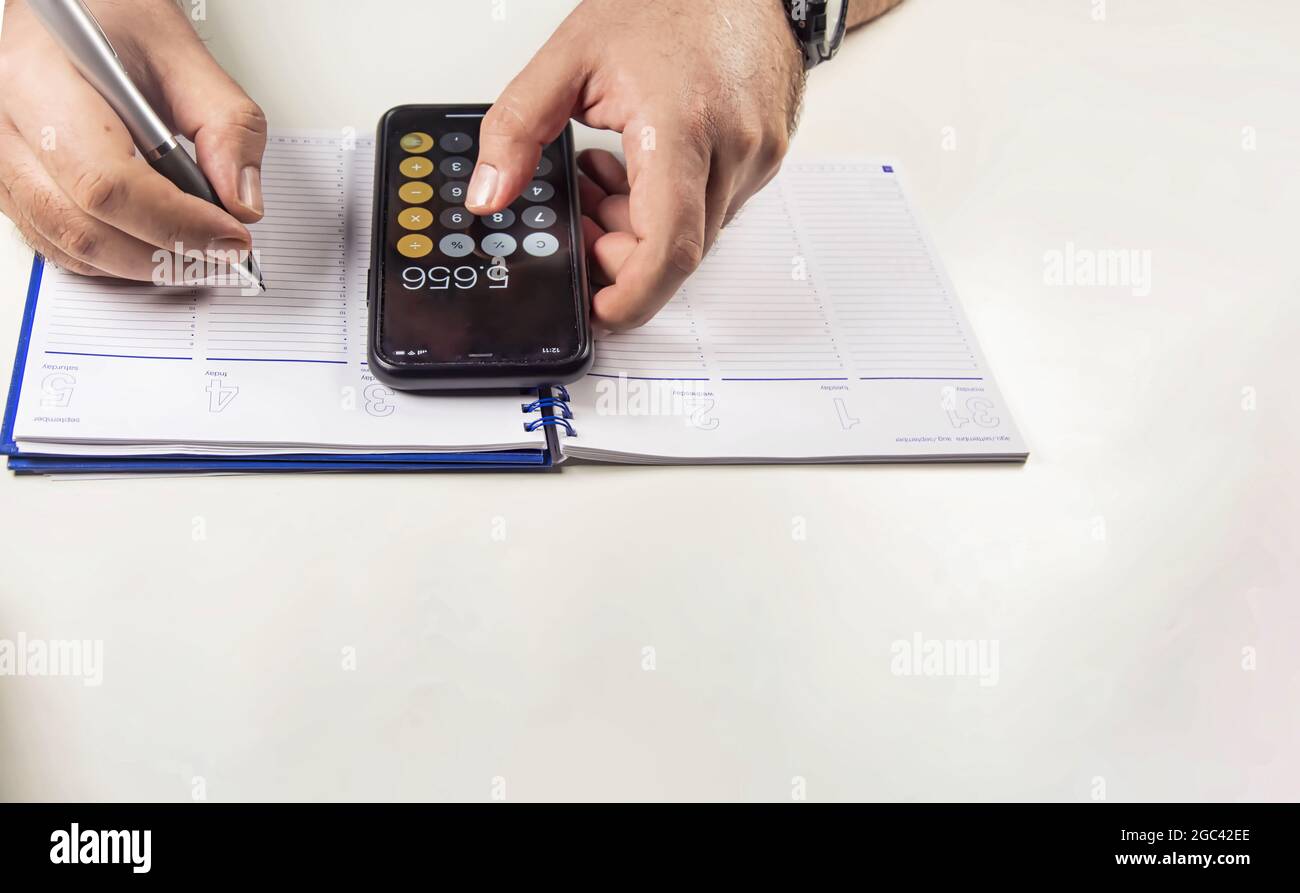 Man doing calculations with his mobile phone calculator and writing in ...
