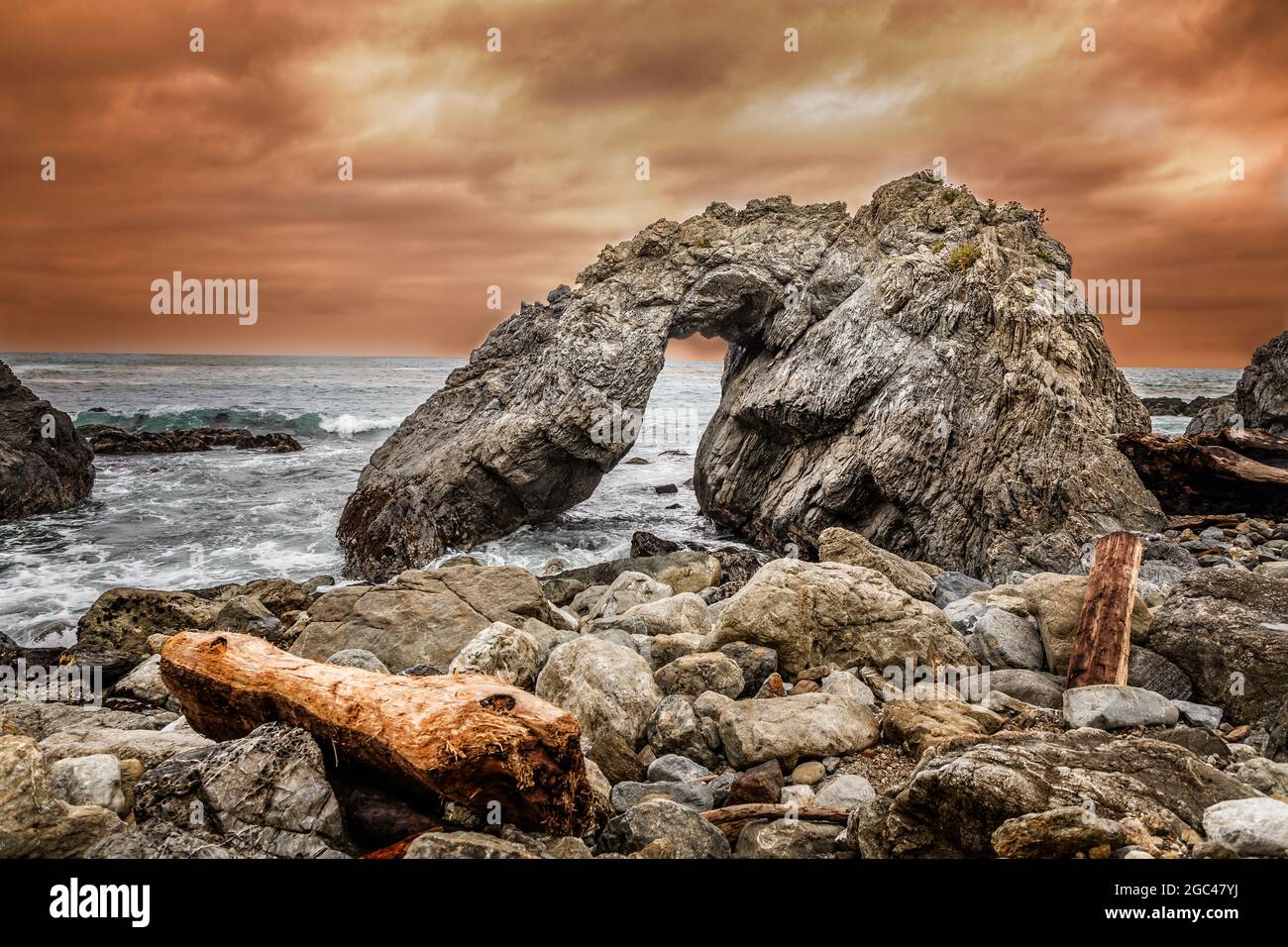 Rock with an arch and driftwood on a California beach Stock Photo - Alamy