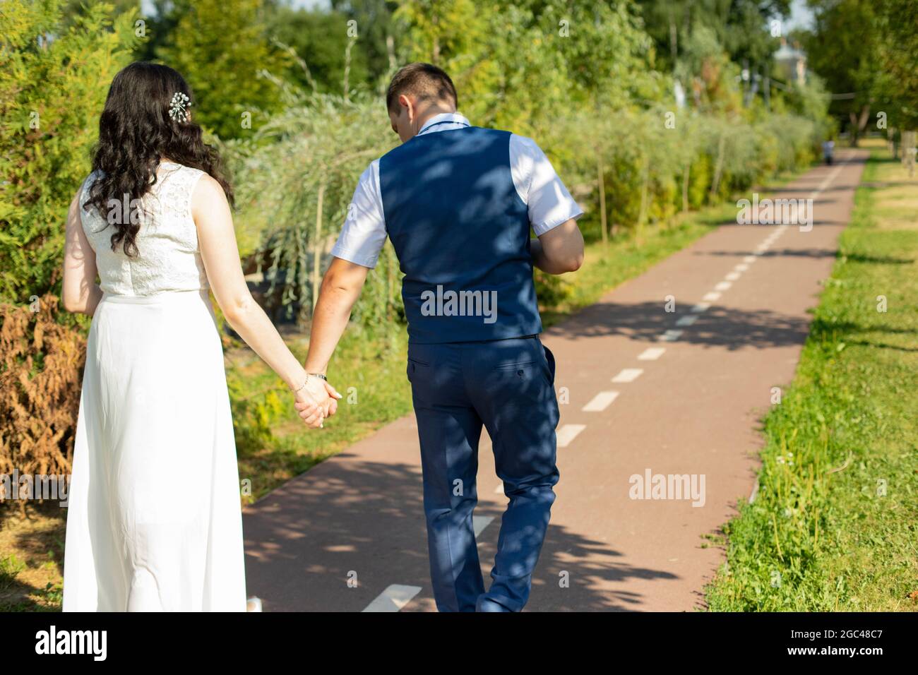 The newlyweds walk along the park path holding hands. A guy and a girl ...