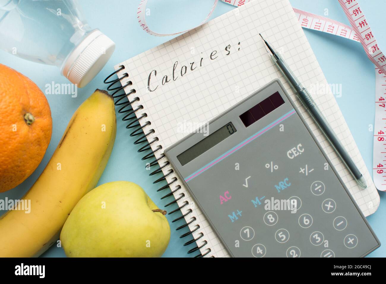 Paper notebook with word CALORIES, calculator, pen, bottle of water ...
