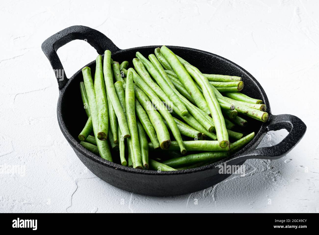 Green string bean set, in frying cast iron pan, on white stone ...