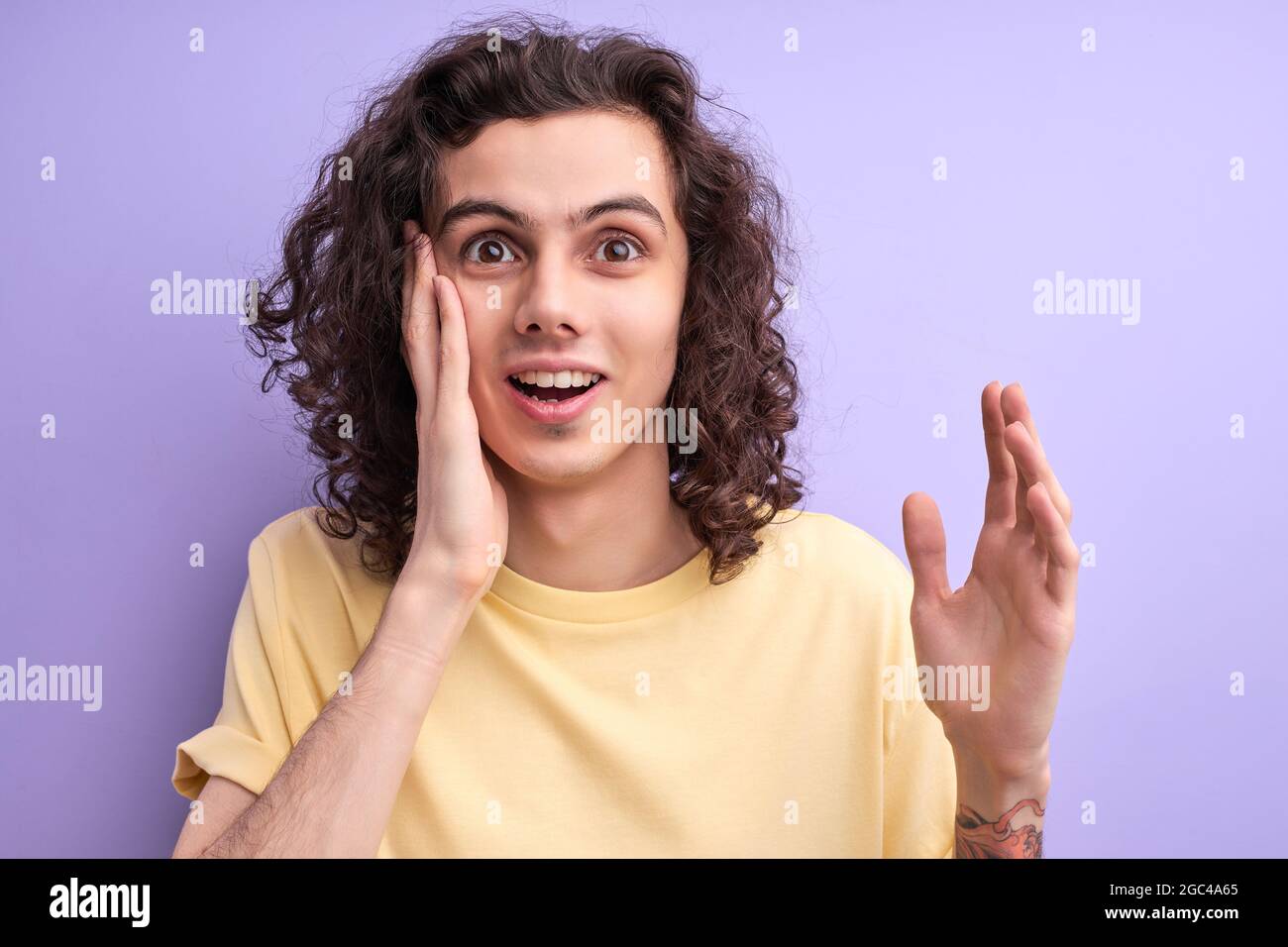 Shocked guy in casual yellow t-shirt isolated on purple background ...