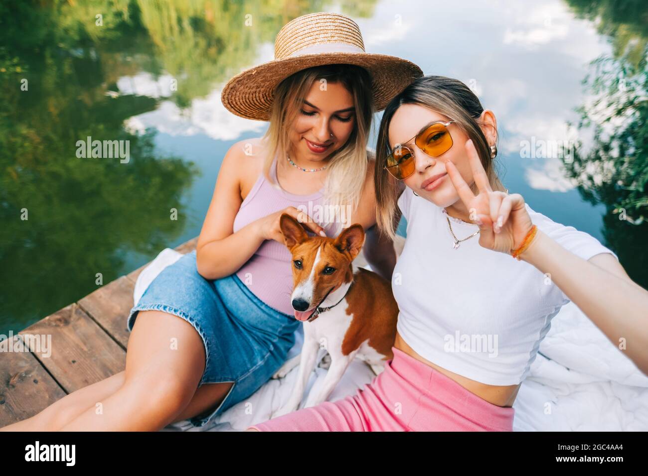 Portrait of two cheerful women friends resting outdoor on lake pier ...