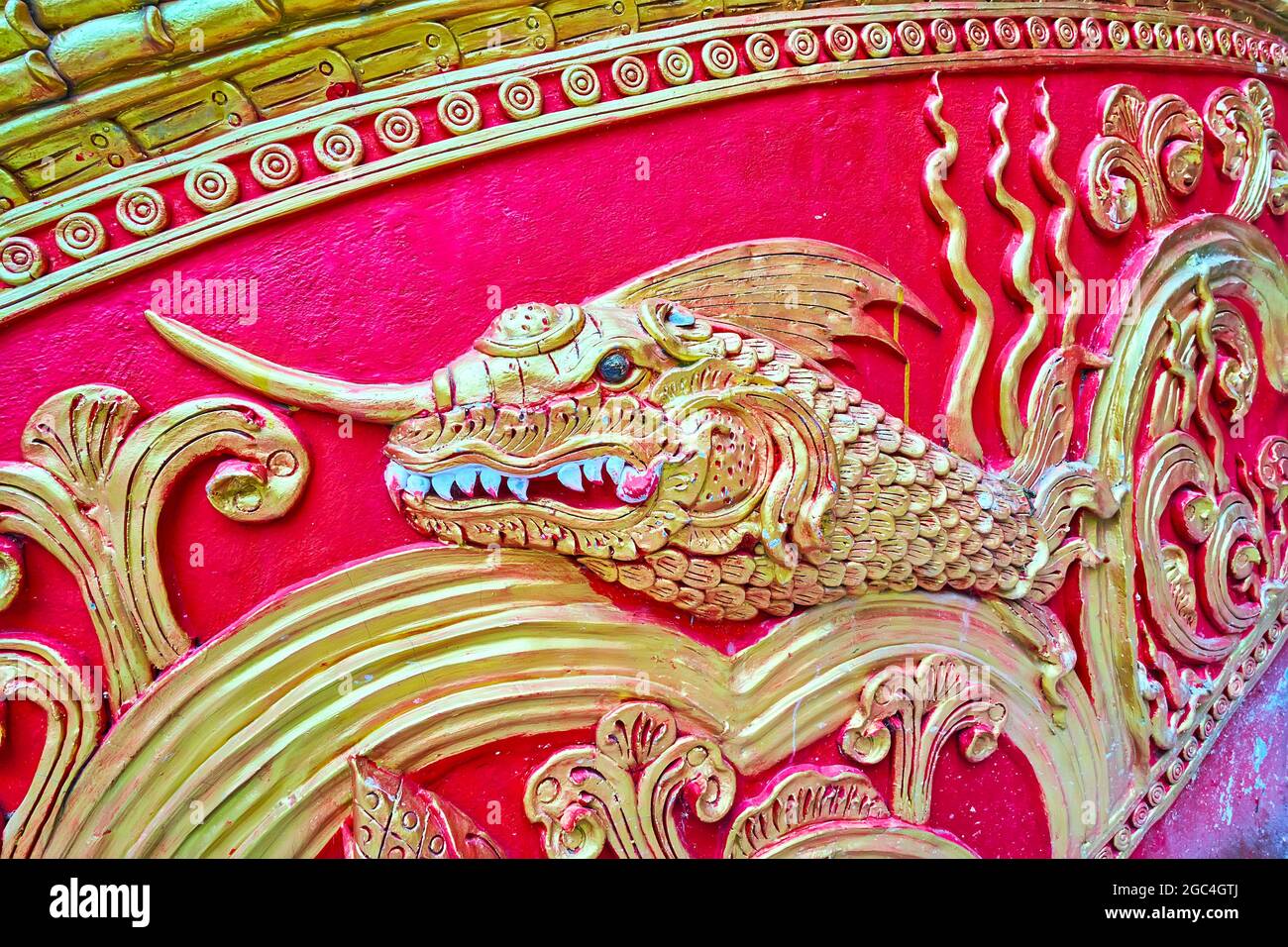The gilt relief of a Thai mythical one-horned fish amid the gilt waves ...