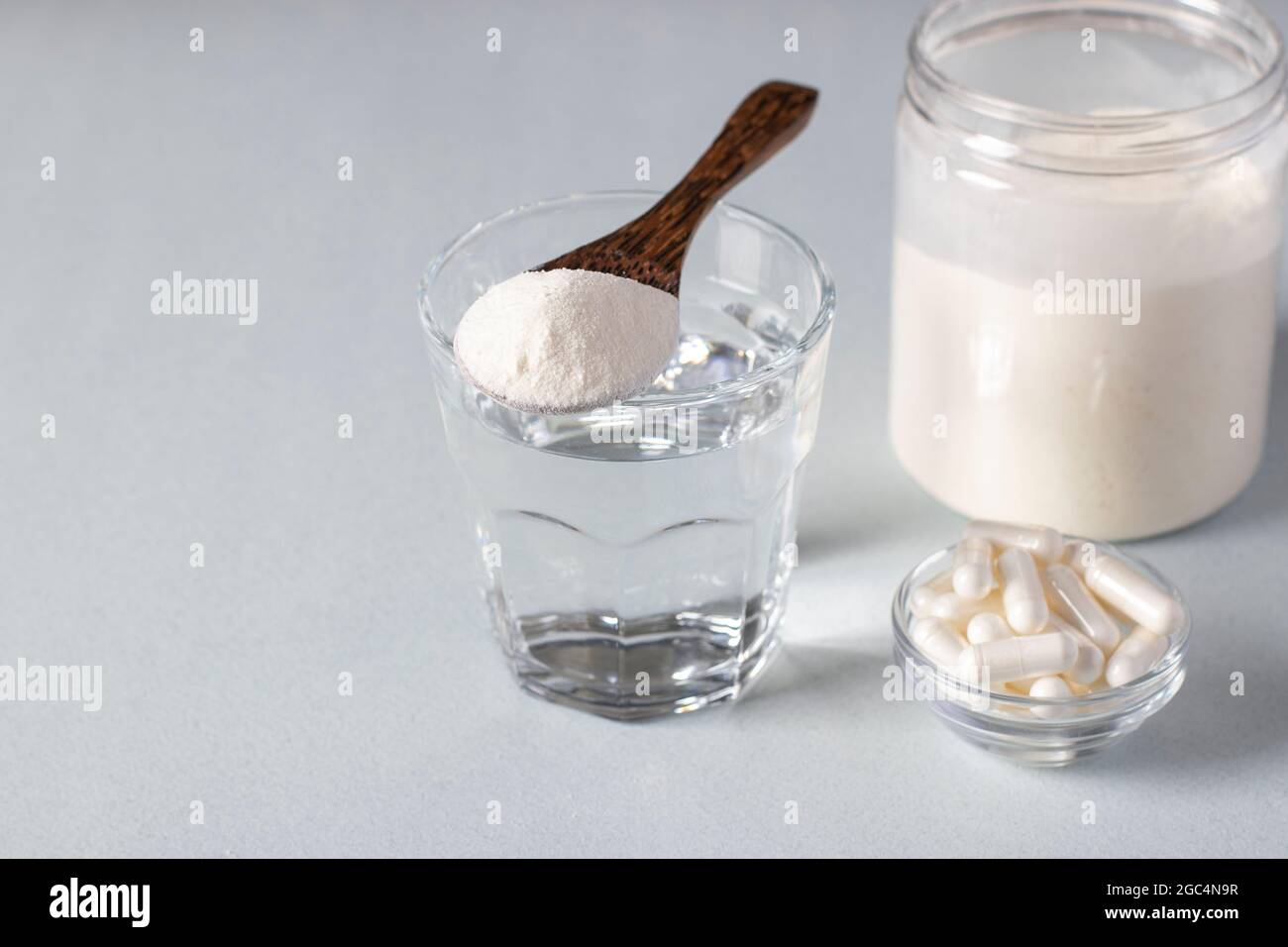 Collagen powder in spoon on glass of water, collagen capsules and jar ...