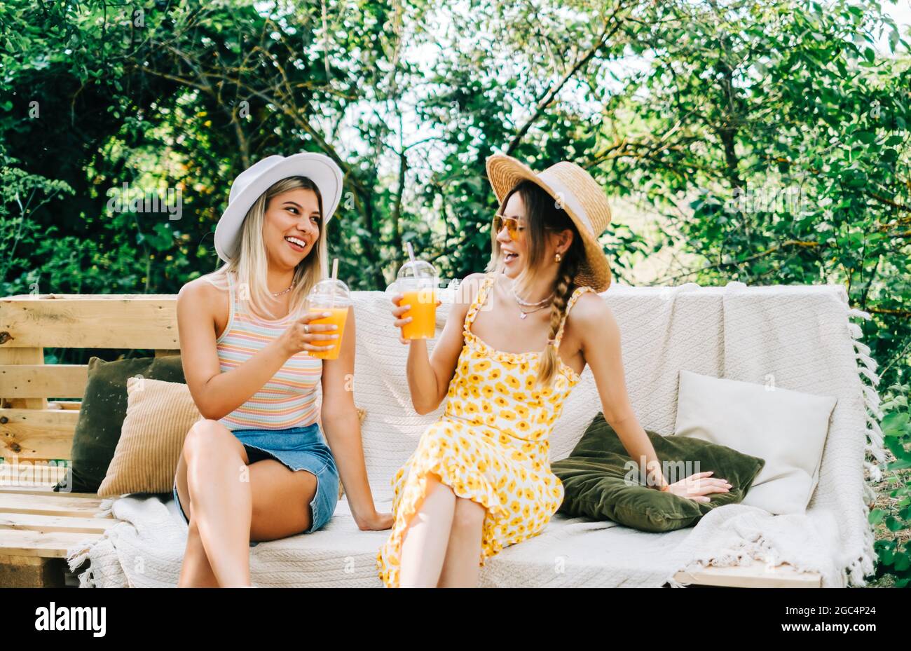 Friends sitting on a sofa in the backyard and drinking orange lemonade ...