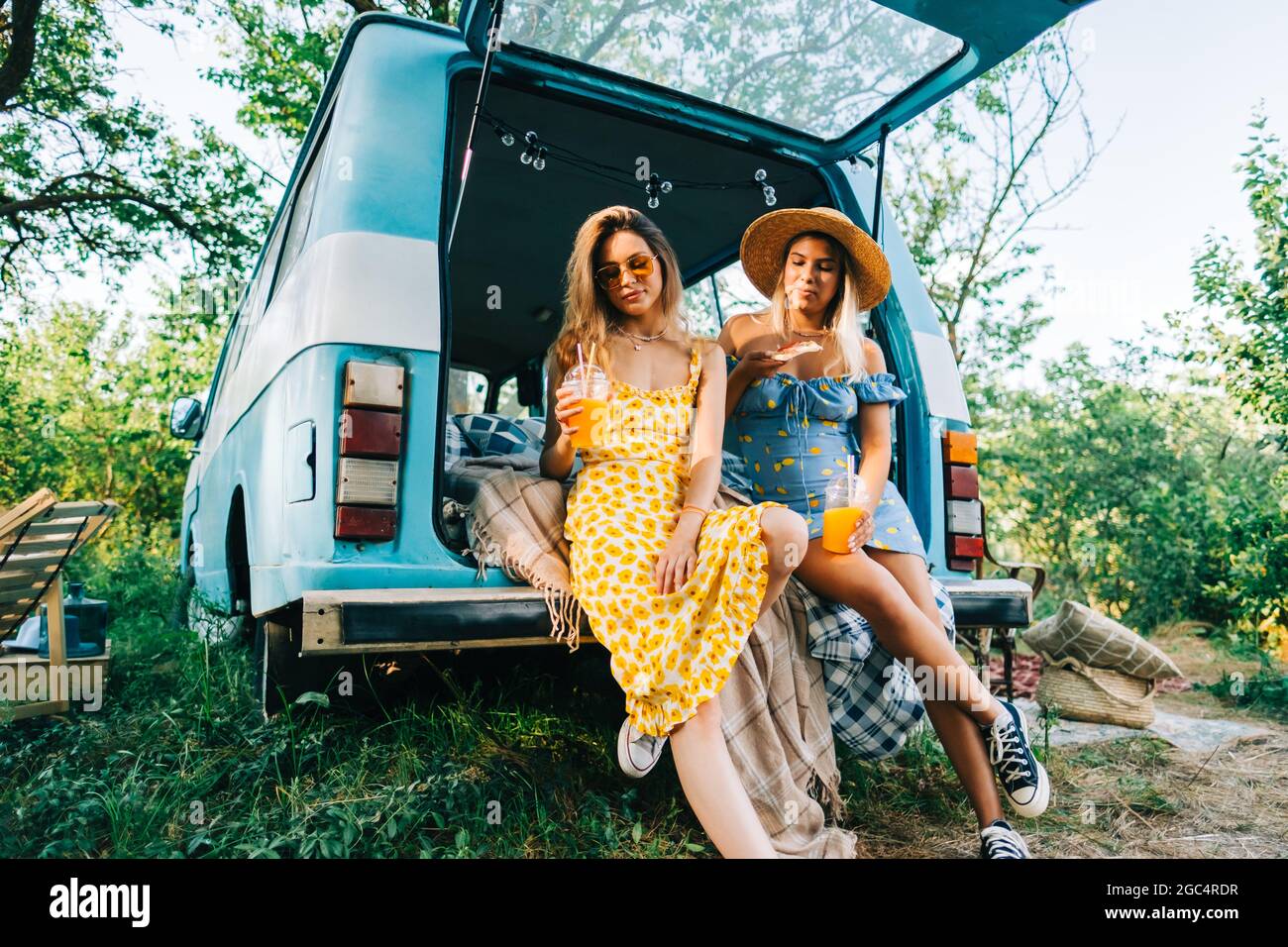 Two attractive cheerful women drinking lemonade near van and eating ...