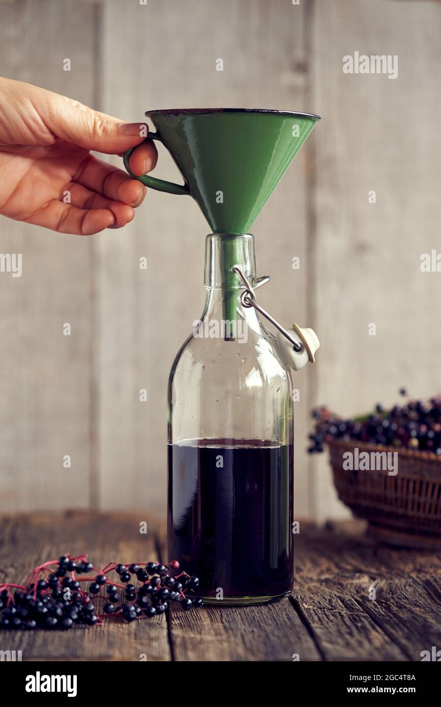 Black elder syrup in a bottle with fresh elderberries, with a hand ...