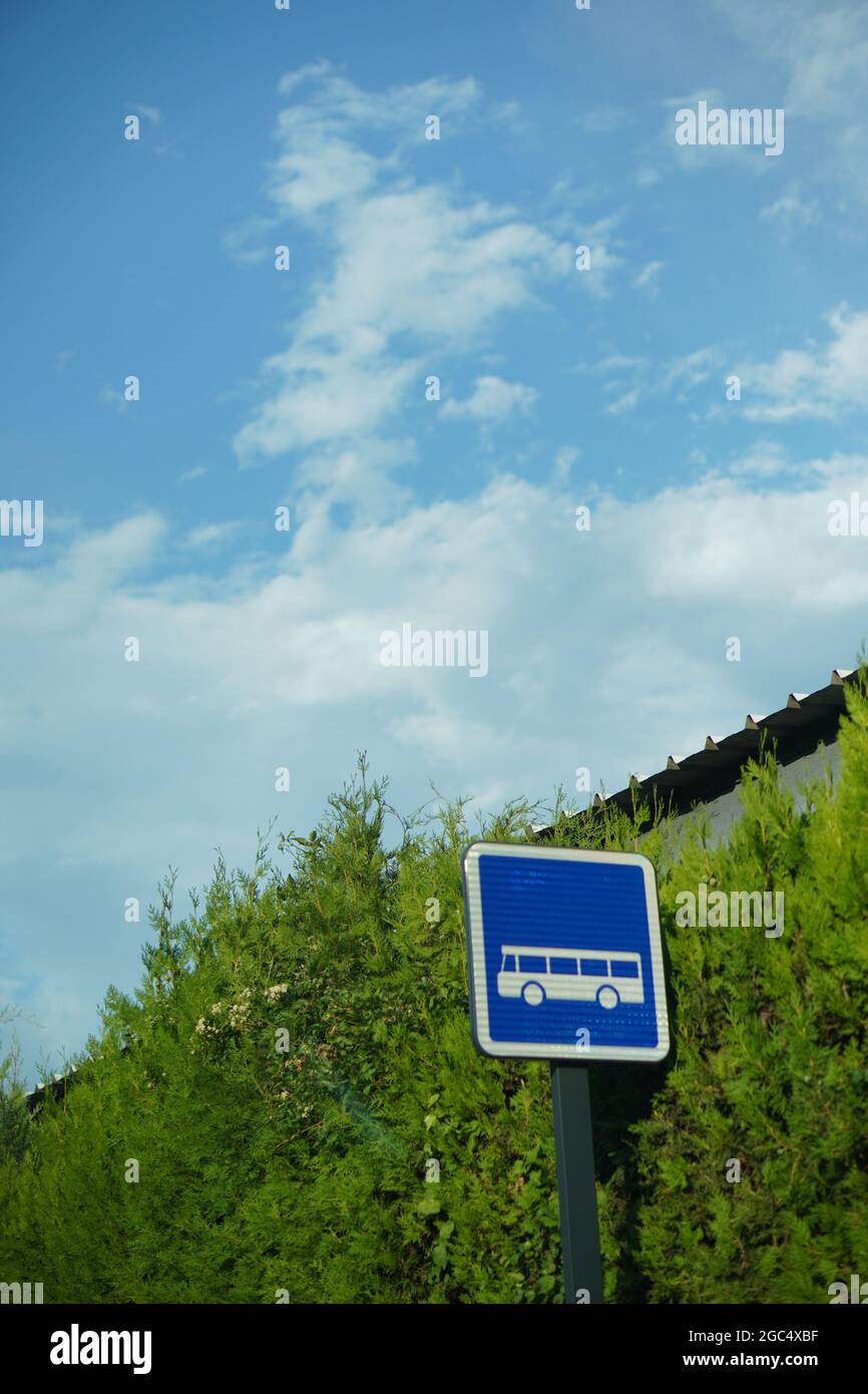 Vertical shot of a bus stop sign near the trees under a blue cloudy sky ...