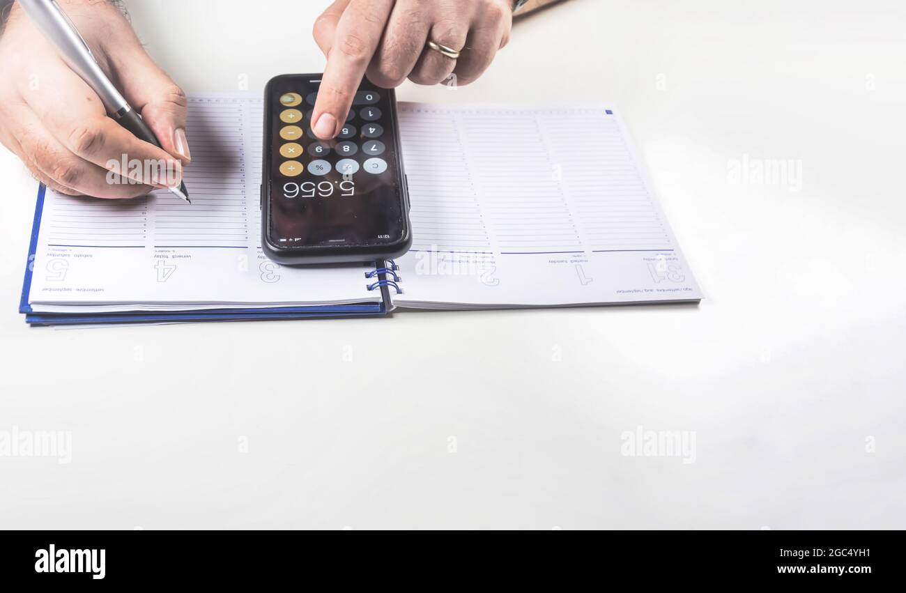 Man doing calculations with his mobile phone calculator and writing in ...