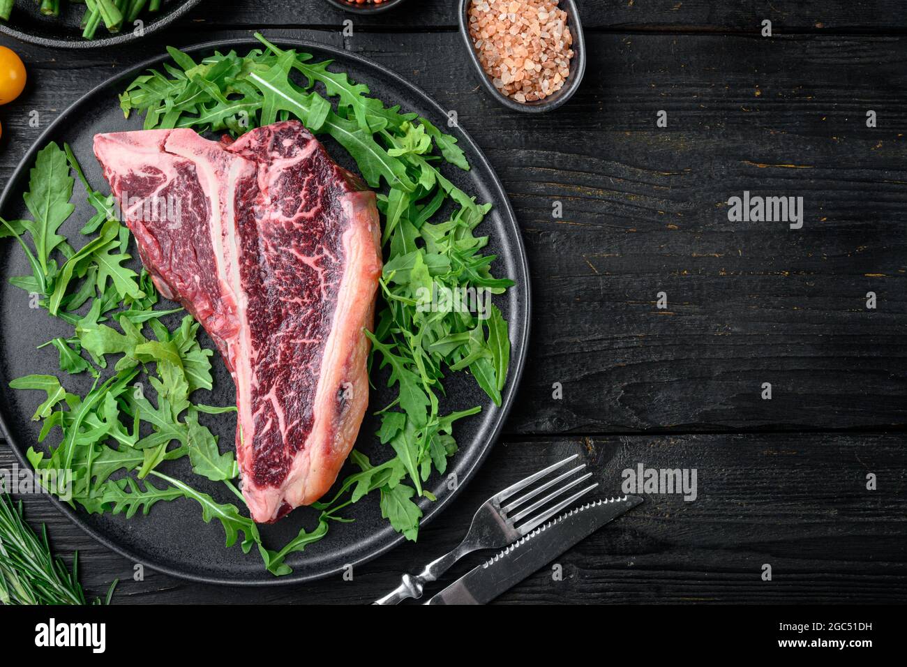 Big raw porterhouse steak with spices and ingredients set, on black ...