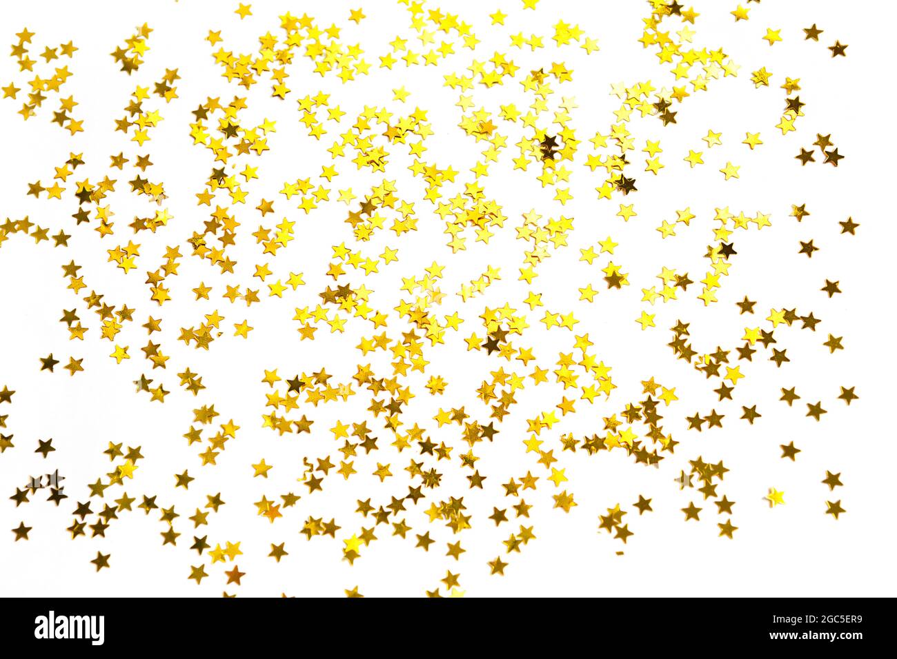Gold sequins in the shape of stars shimmer on a white background ...