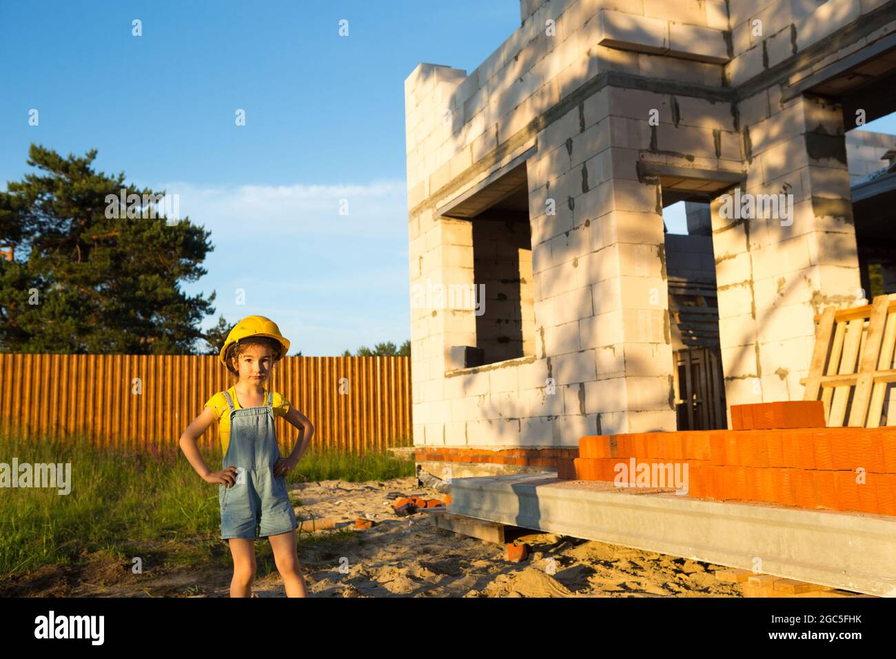 A little girl in a yellow hardhat is playing builder on the ...