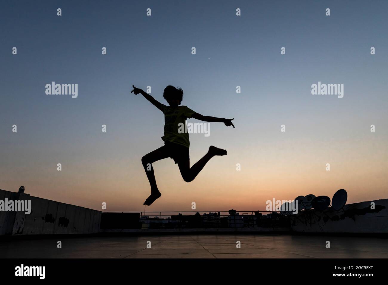 Silhouette of a young boy jumping in the air with his arms and legs ...