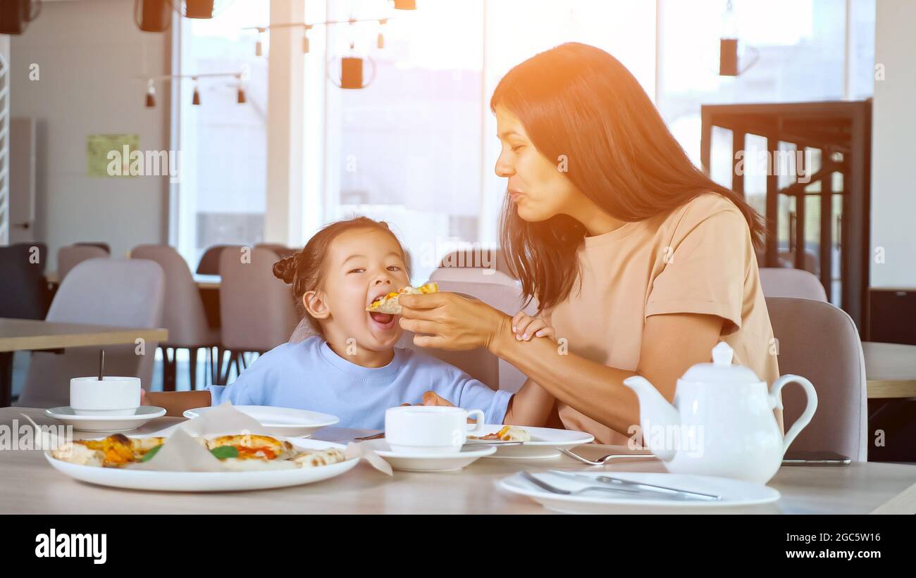 Lady mom holds pizza slice and daughter eats in cafe Stock Photo - Alamy